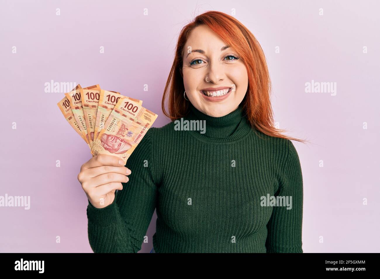 Beautiful redhead woman holding 100 mexican pesos banknotes looking ...