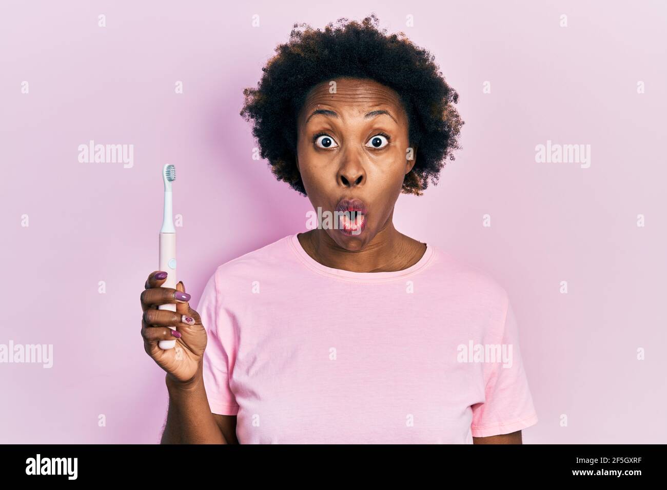 Young african american woman holding electric toothbrush scared and ...