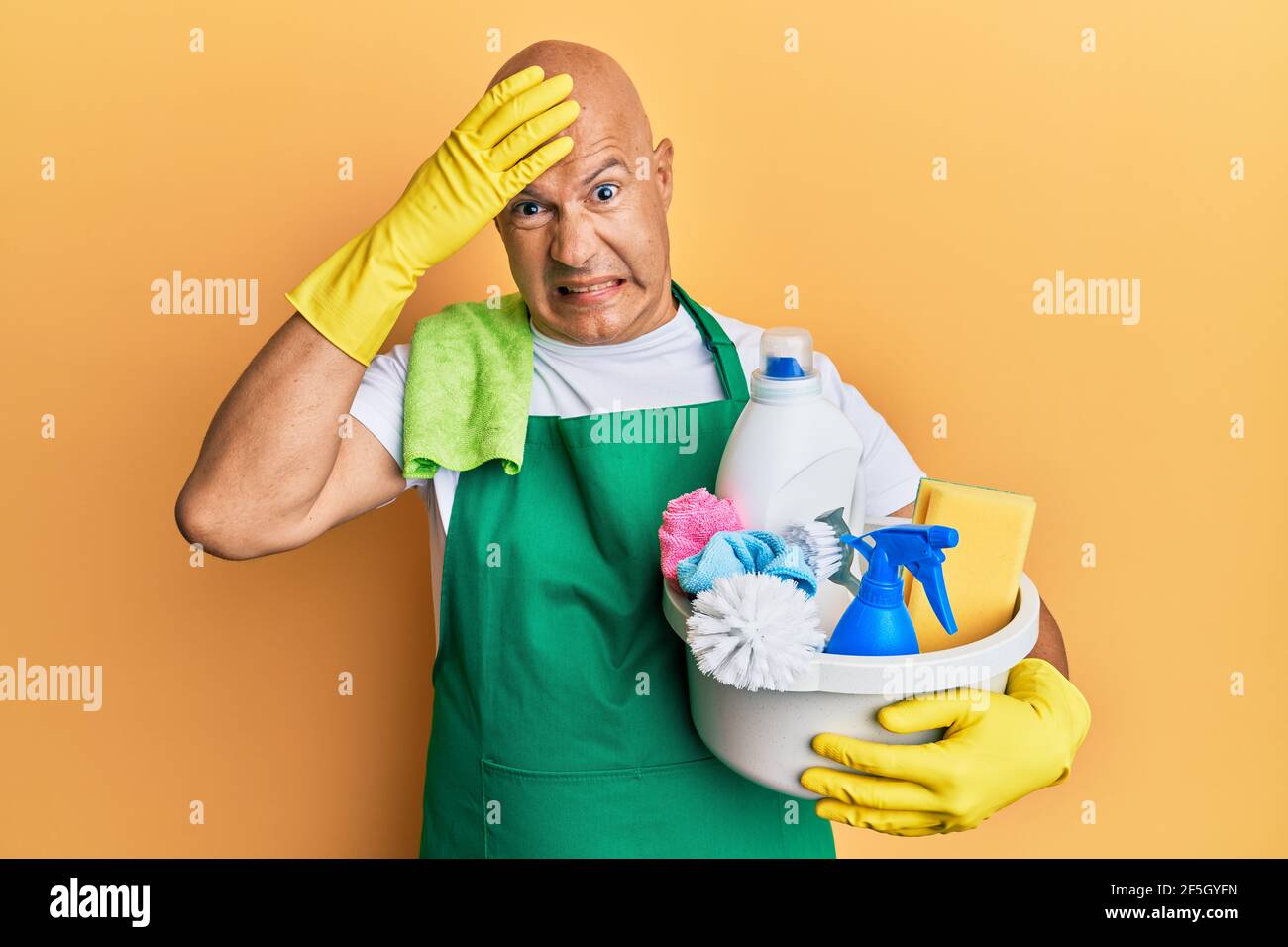 Middle age bald man wearing cleaner apron holding cleaning products ...