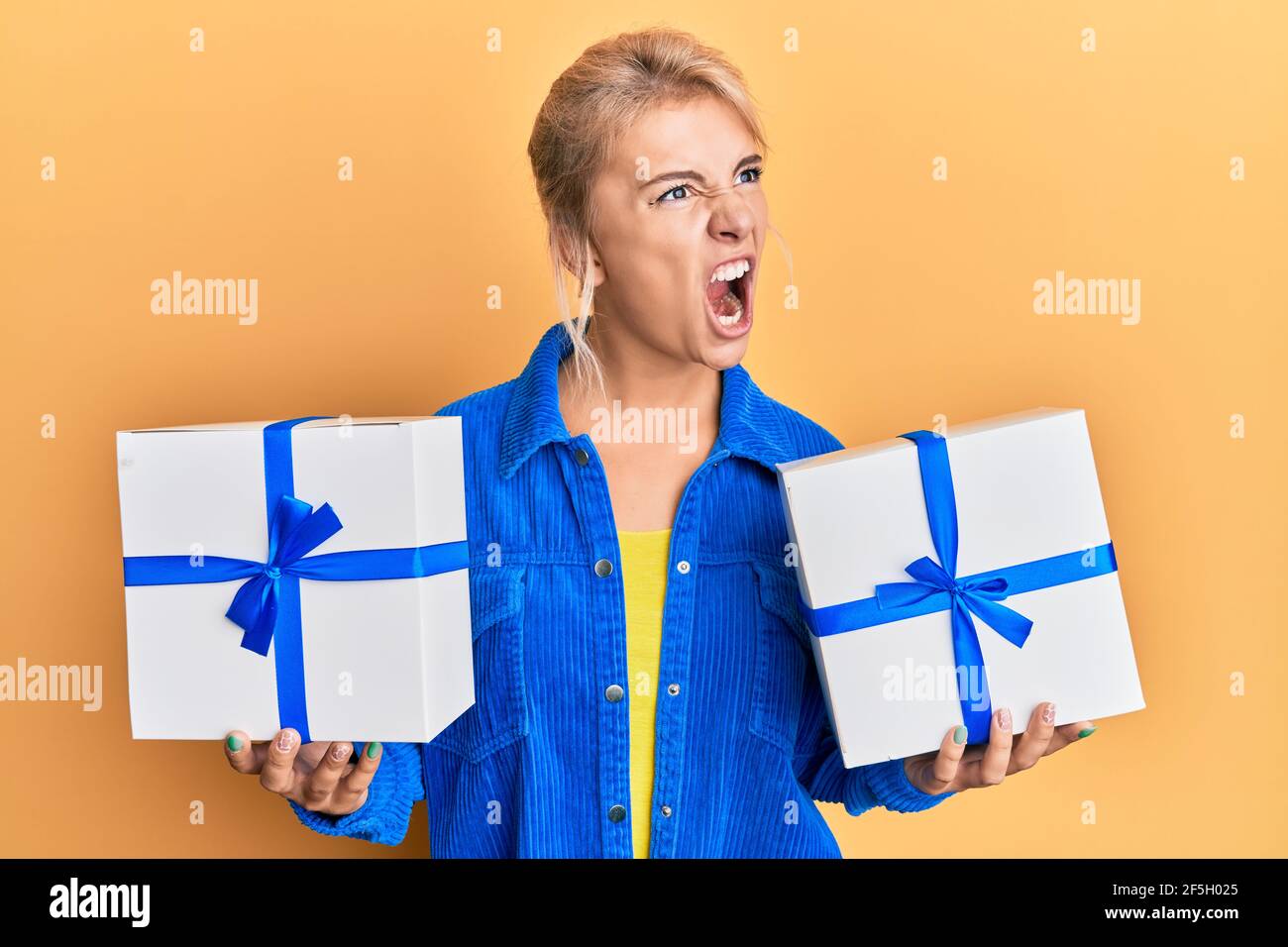 Young blonde girl holding gifts angry and mad screaming frustrated and ...