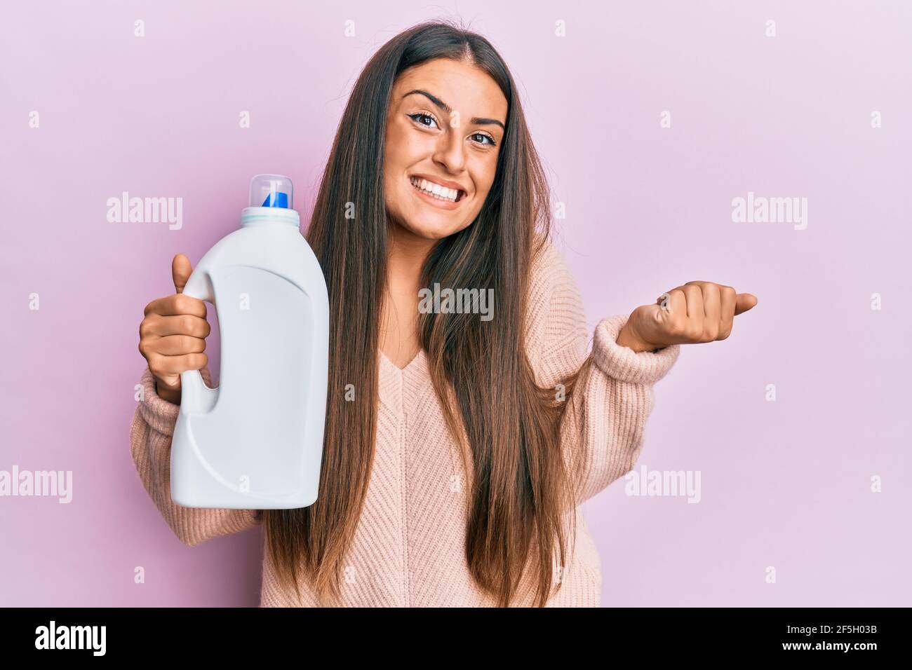 Beautiful hispanic woman holding laundry detergent bottle screaming ...