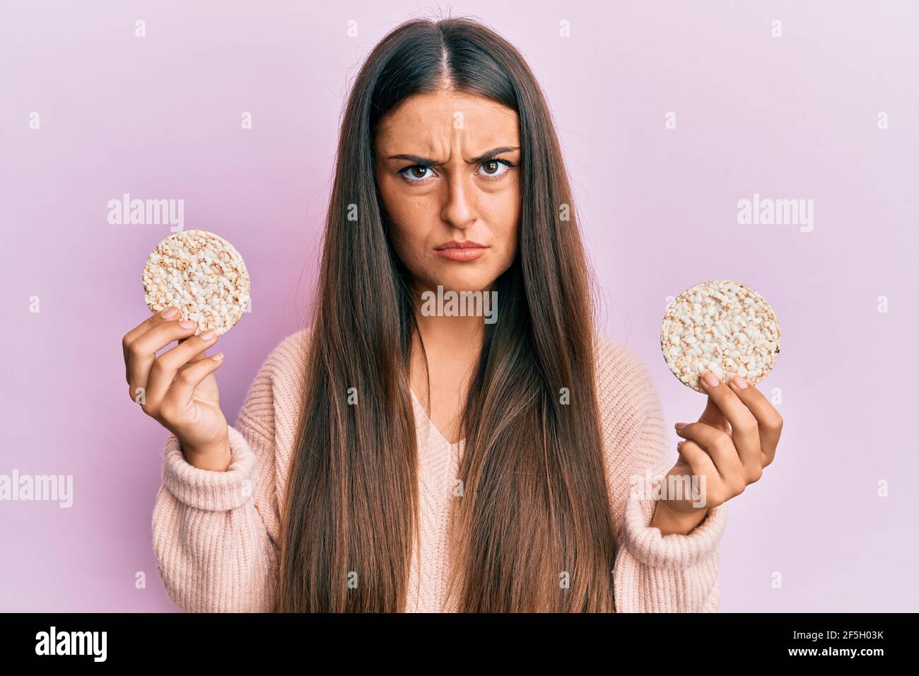Beautiful hispanic woman eating healthy rice crackers skeptic and ...