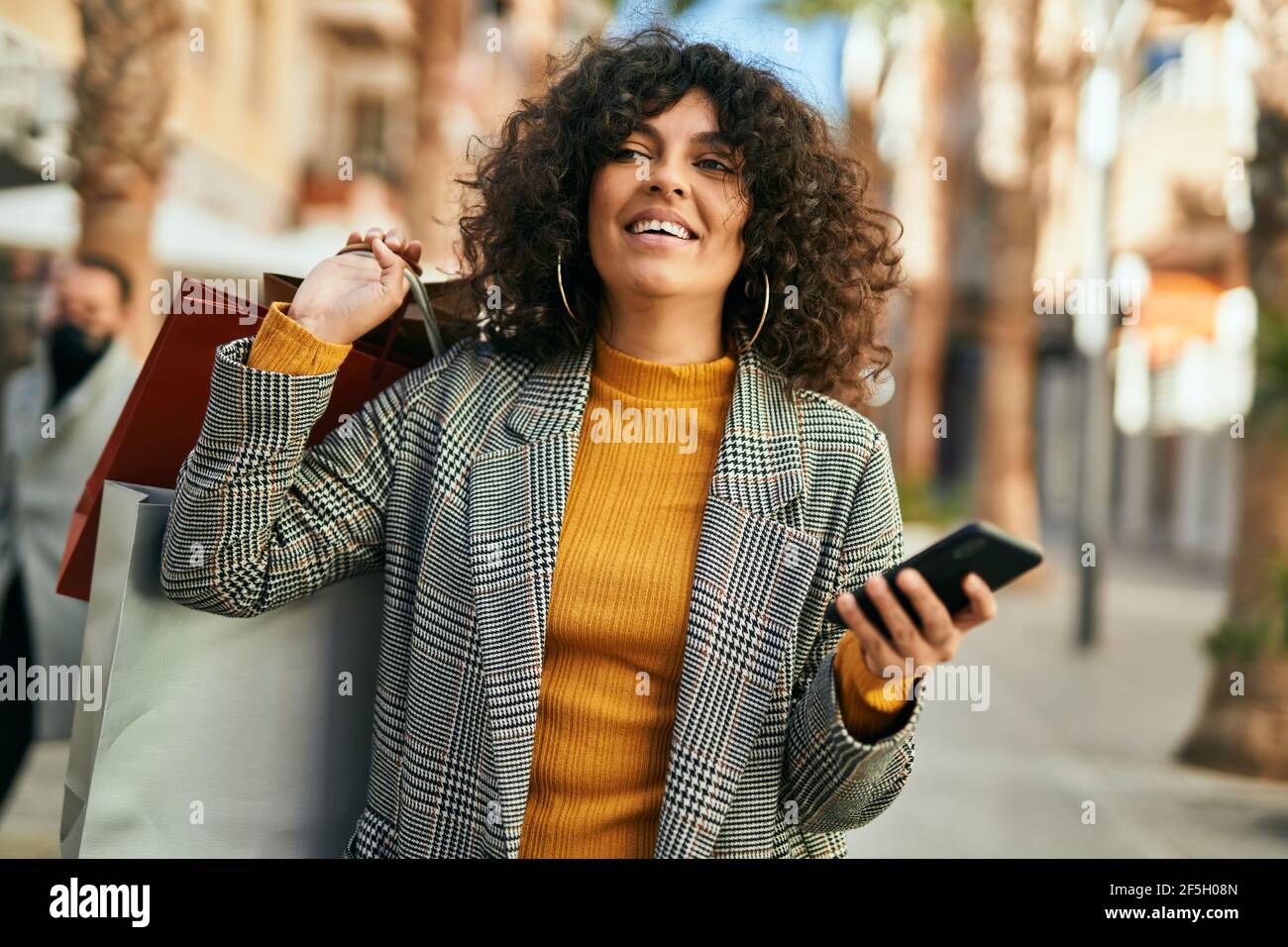 Young hispanic woman going shopping and using smatphone at the city ...