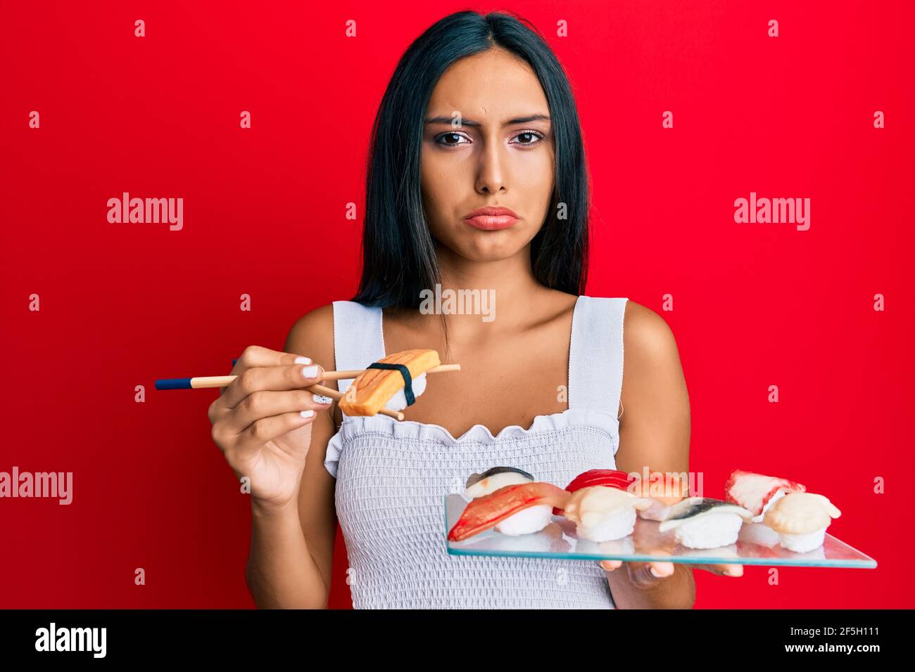 Young brunette woman eating omelet sushi using chopsticks depressed and ...