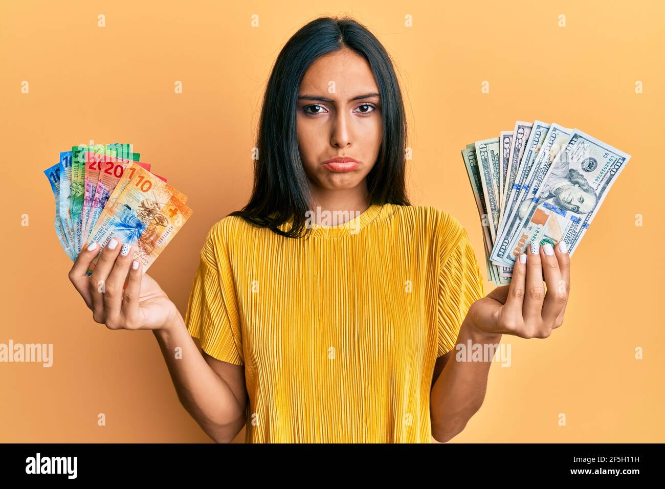 Young brunette woman holding bunch of dollars and swiss francs ...