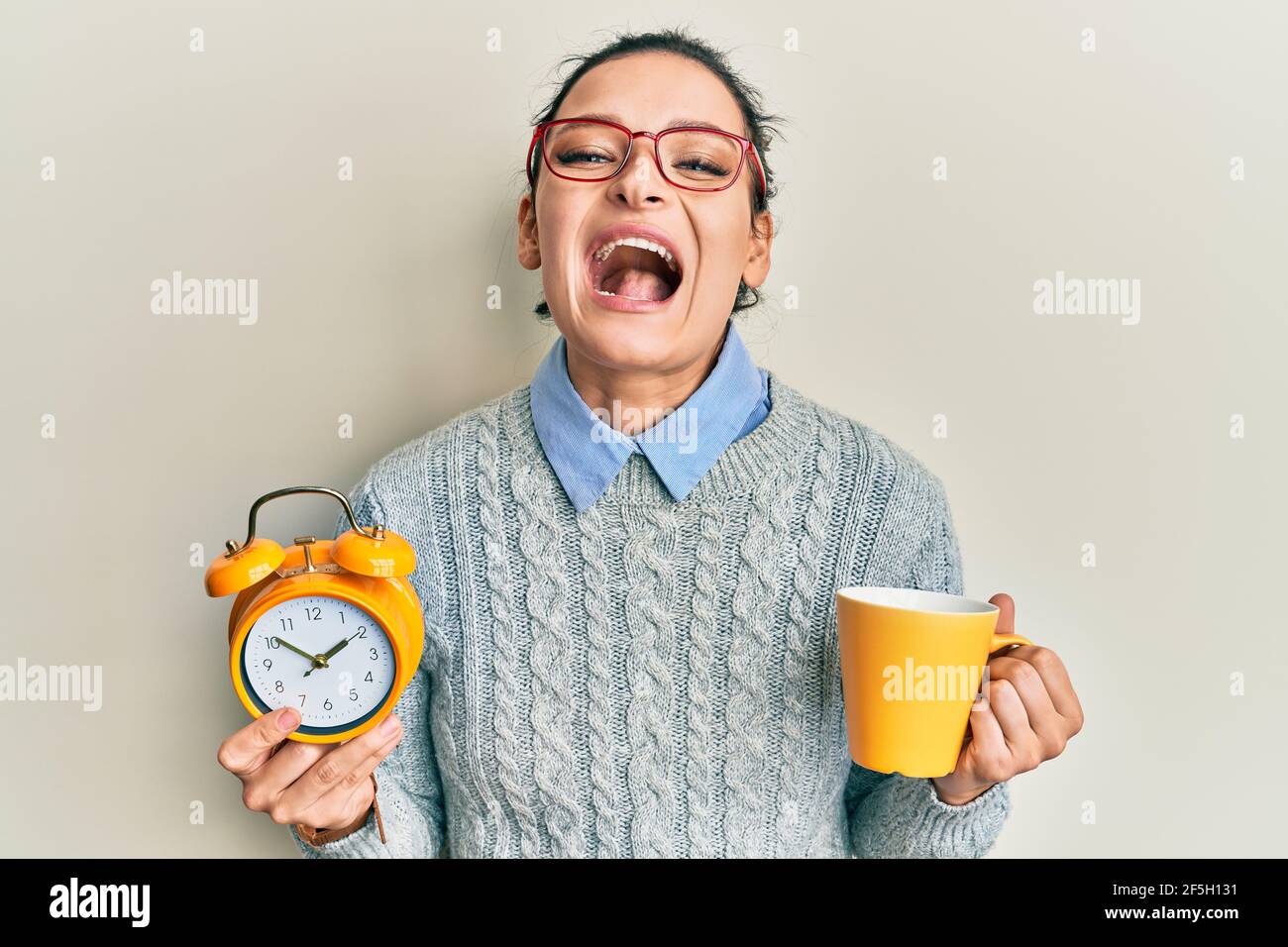 Young caucasian woman holding alarm clock drinking coffee angry and mad ...