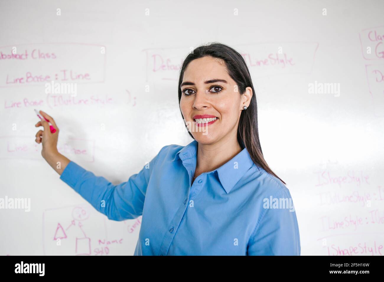 latin Female school teacher looks at camera in classroom speaking ...
