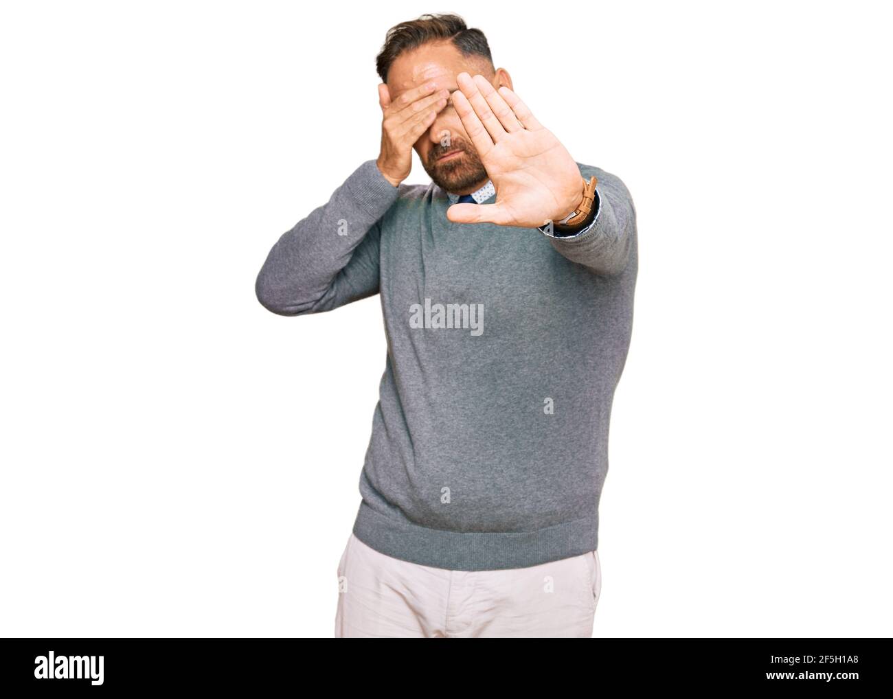 Handsome middle age man wearing business clothes covering eyes with ...