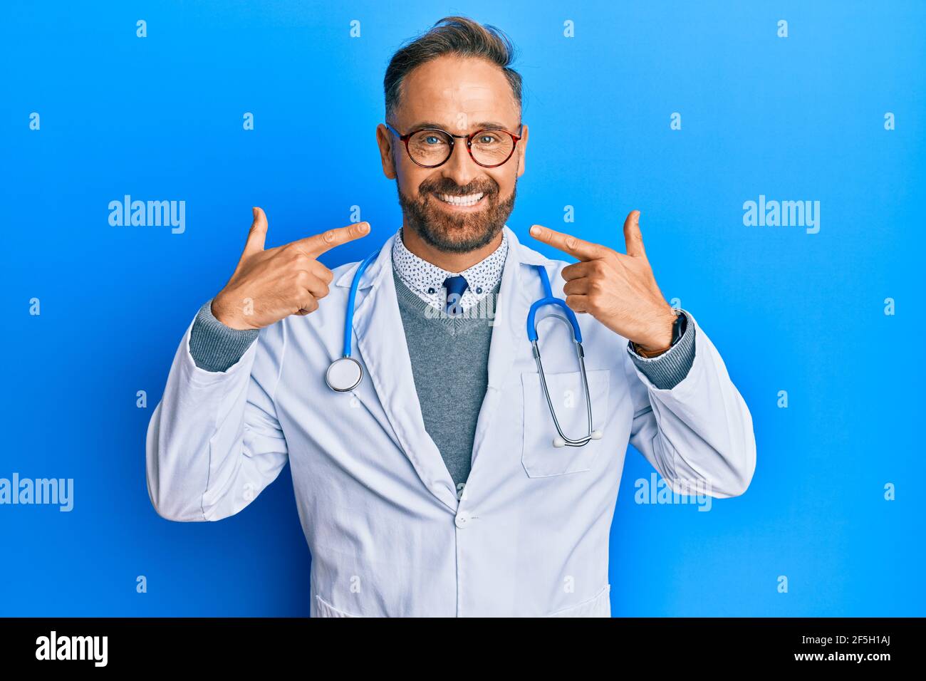 Handsome middle age man wearing doctor uniform and stethoscope smiling ...