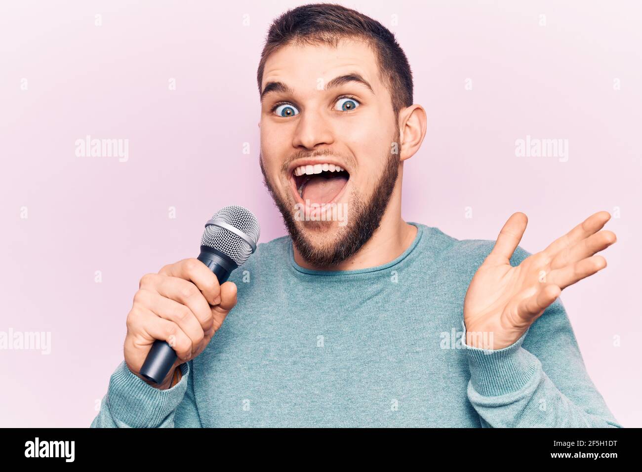 Young handsome man singing song using microphone celebrating ...