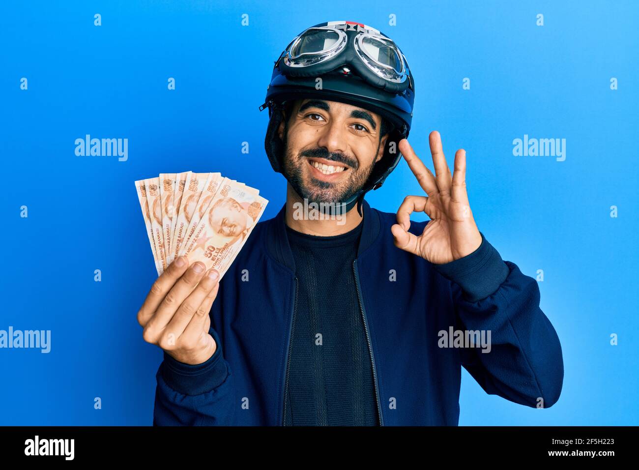 Young hispanic man wearing motorcycle helmet holding turkish lira doing ...