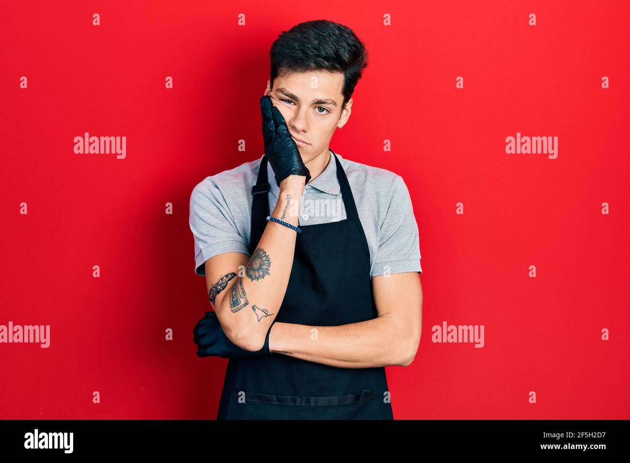 Young hispanic man wearing apron thinking looking tired and bored with ...