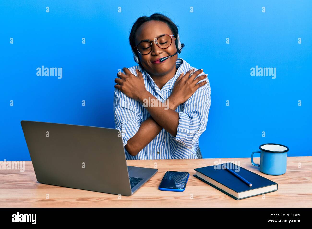 Young african woman wearing call center agent headset hugging oneself ...