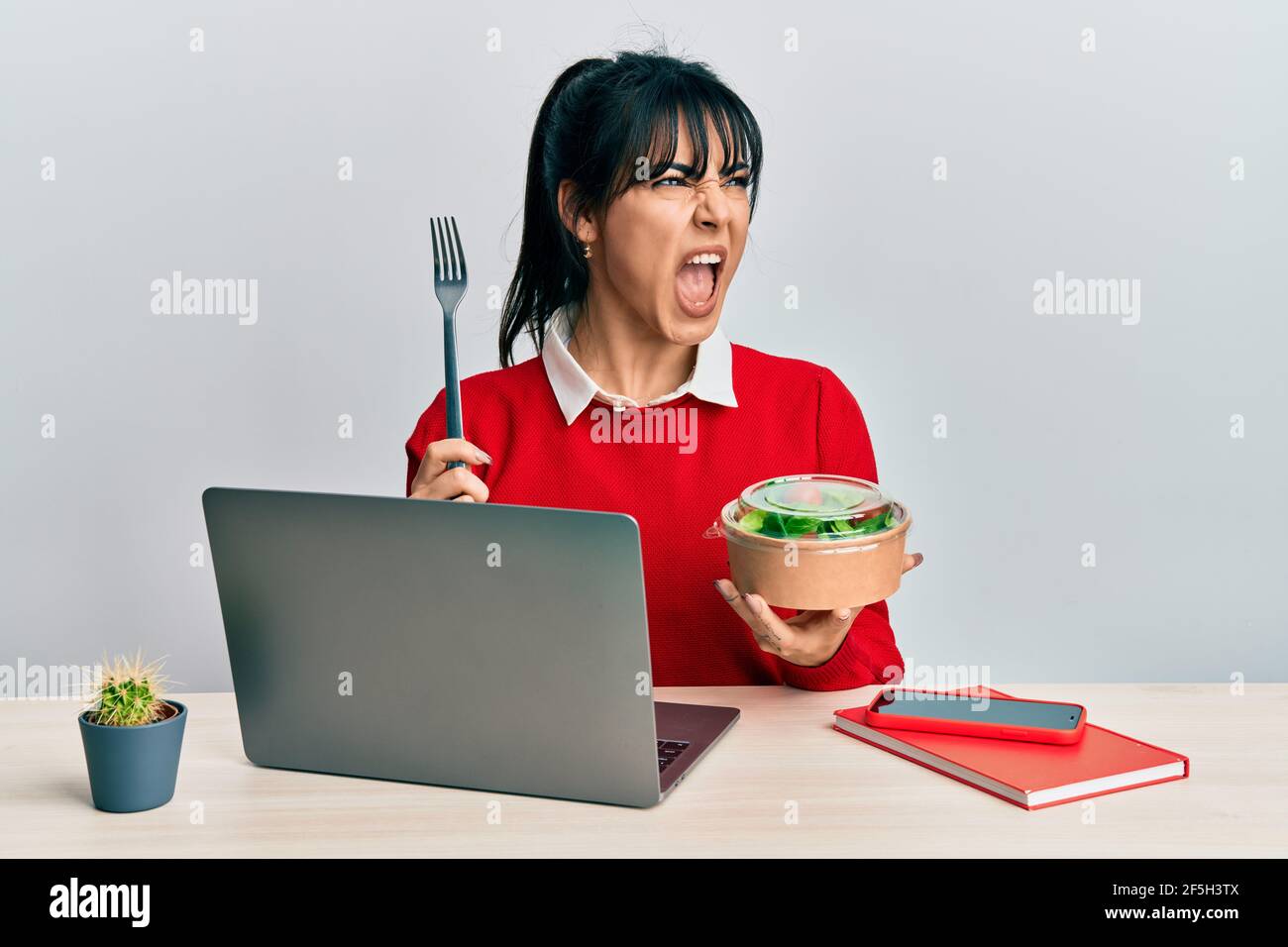 Young brunette woman with bangs working at the office eating healthy ...