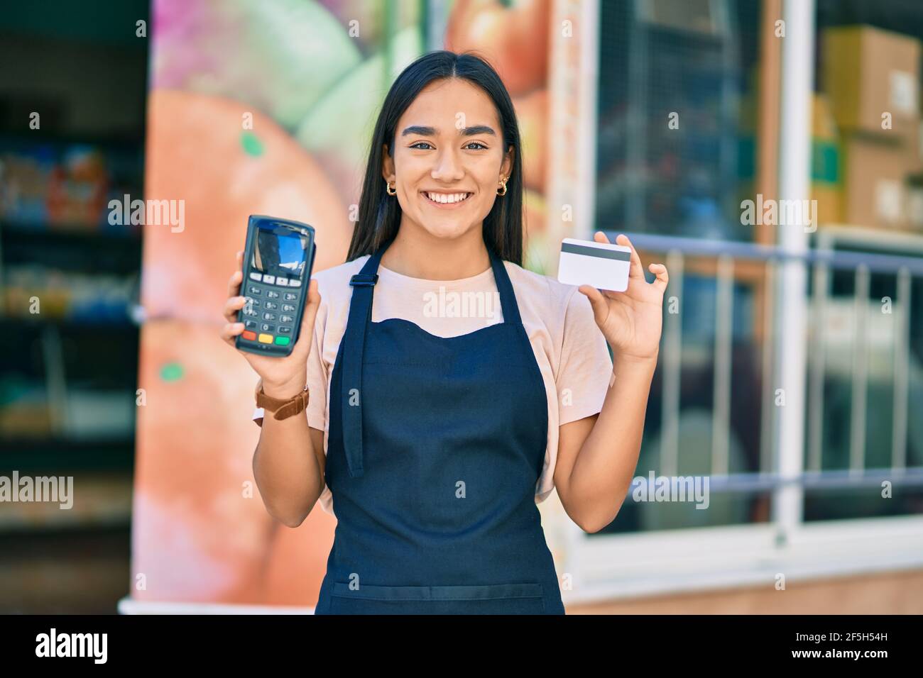 Young latin shopkeeper girl smiling happy holding credit card and ...