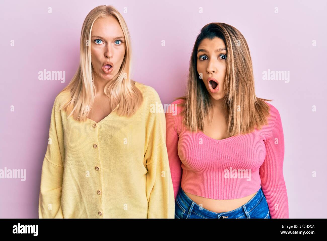 Two friends standing together over pink background afraid and shocked ...