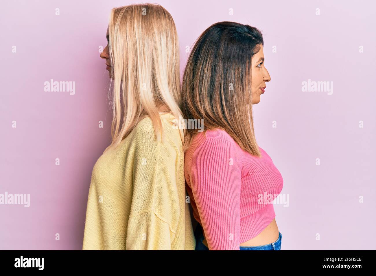 Two friends standing together over pink background looking to side ...