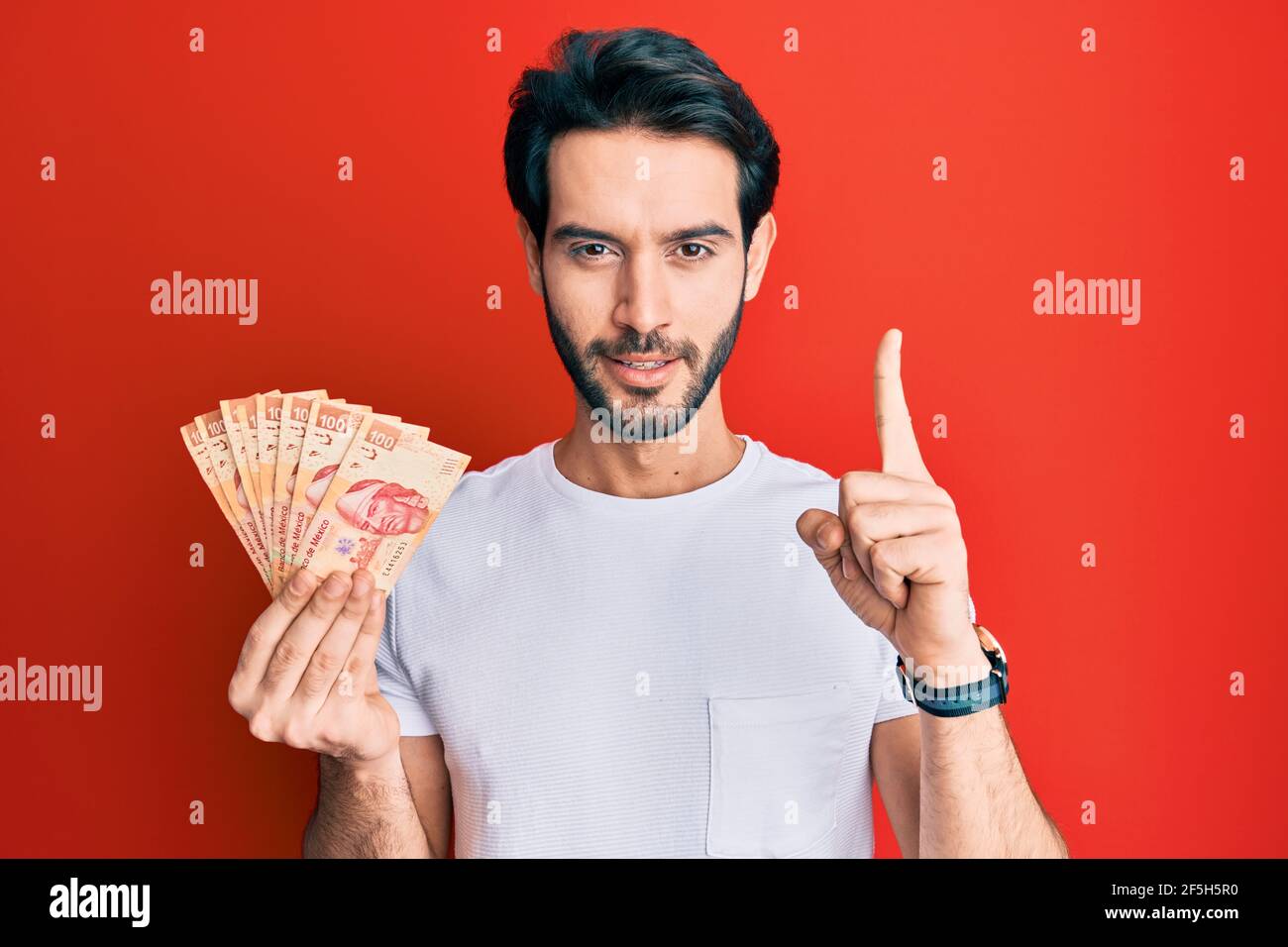Young hispanic man holding mexican pesos smiling with an idea or ...