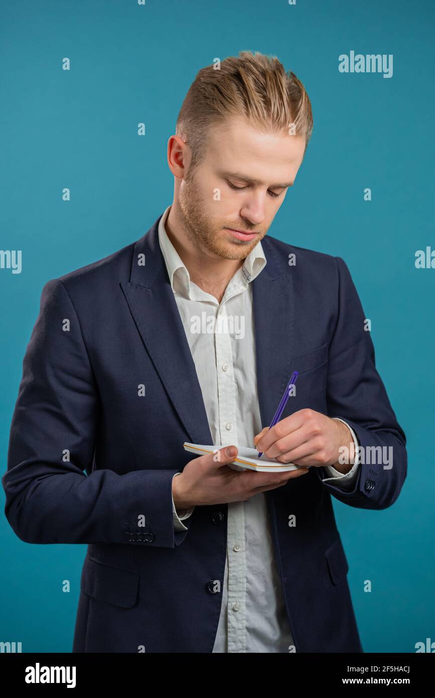 Left-handed young businessman making notes in planner, guy holding pen ...