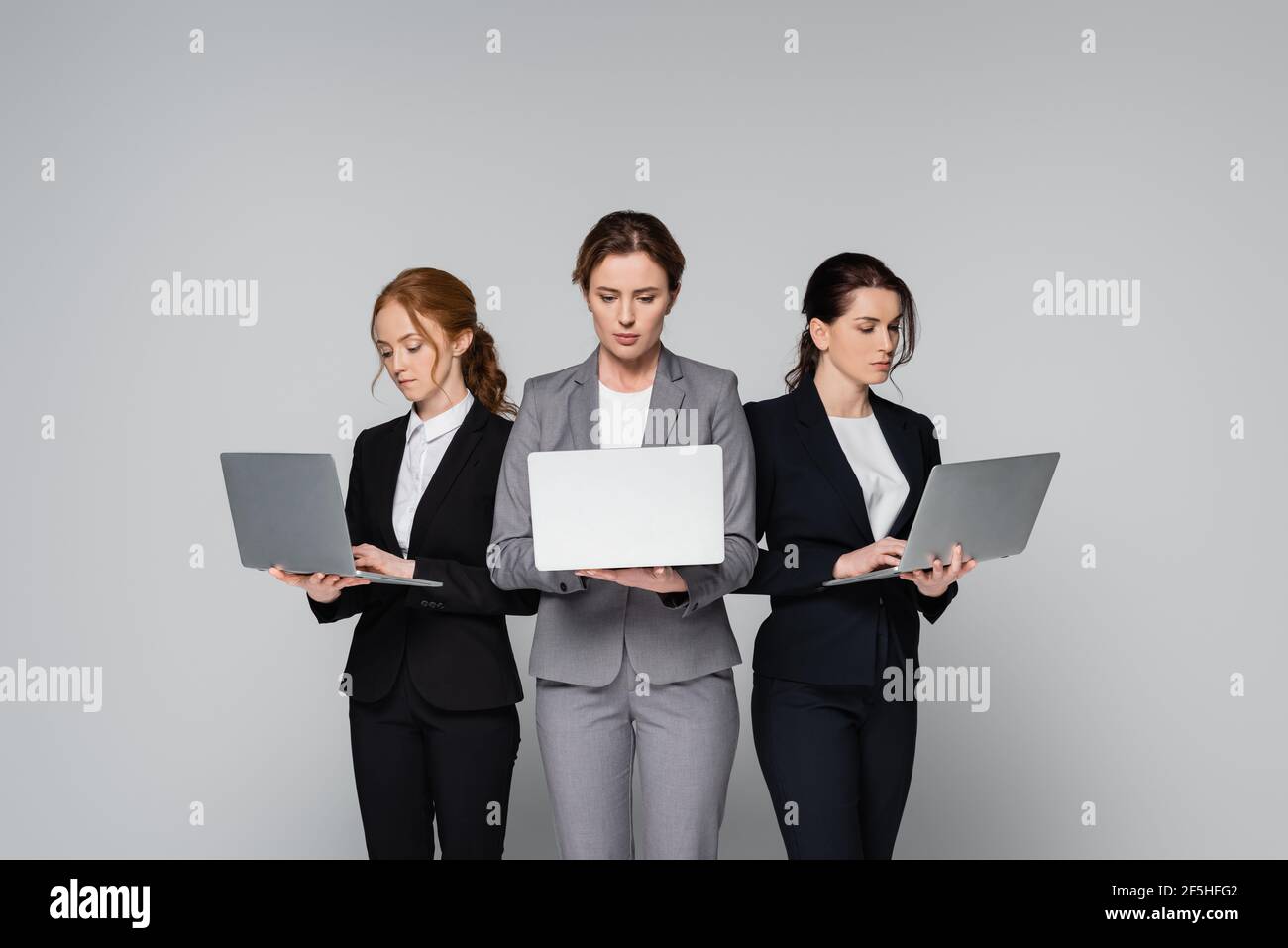 Confident businesswomen using laptops isolated on grey Stock Photo - Alamy