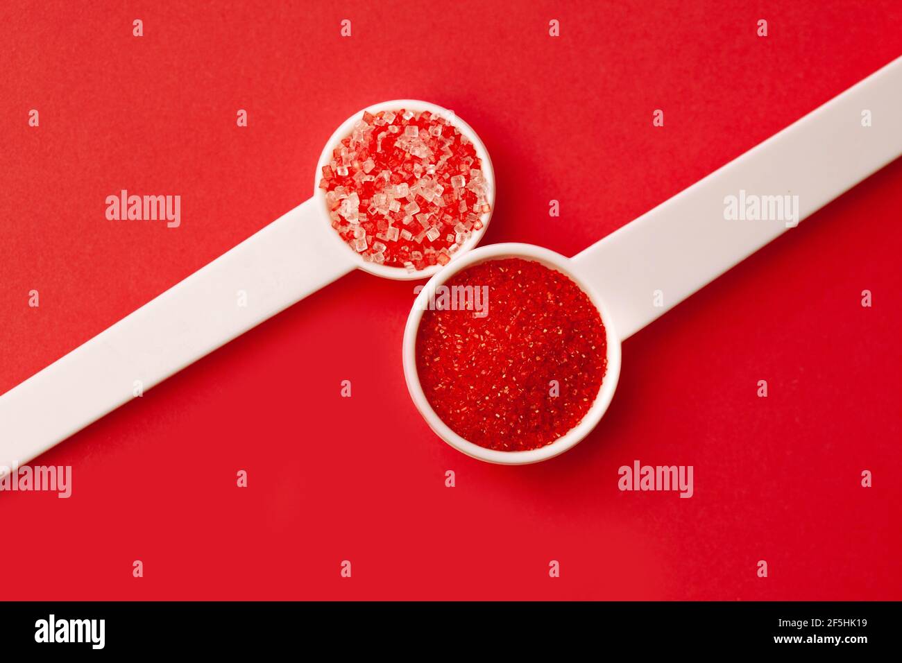 Red colored sugar in white spoon on red background - red crystals edble ...
