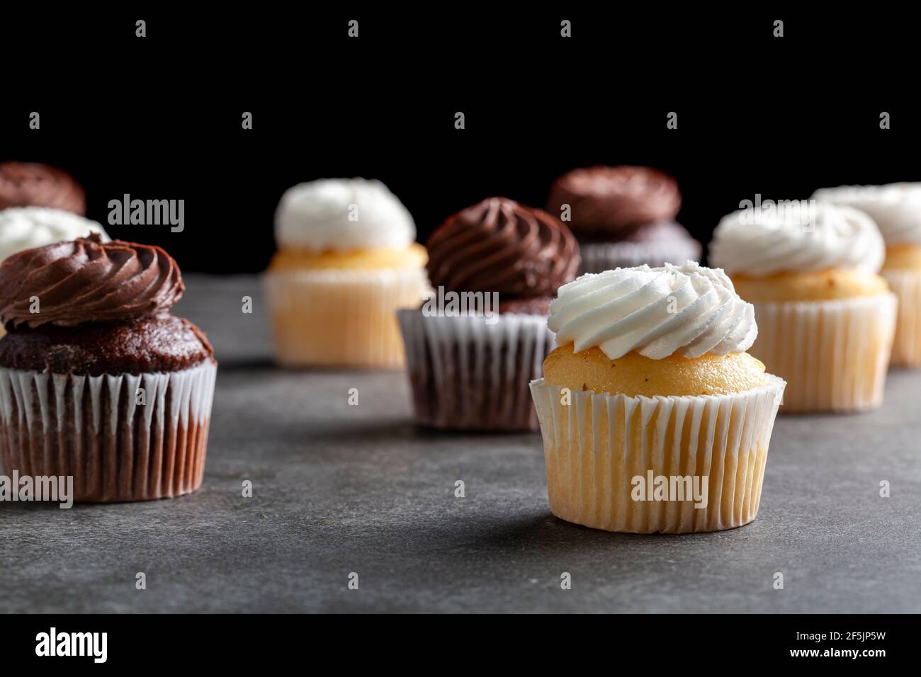 Side view image of vanilla and chocoloate cupcakes on dark stone ...