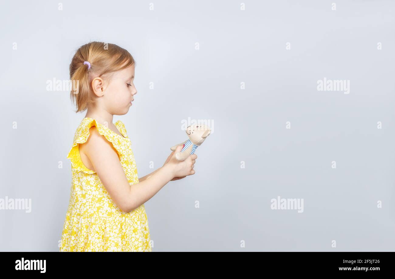 Little Caucasian girl with teddy bear standing sideways to the camera ...