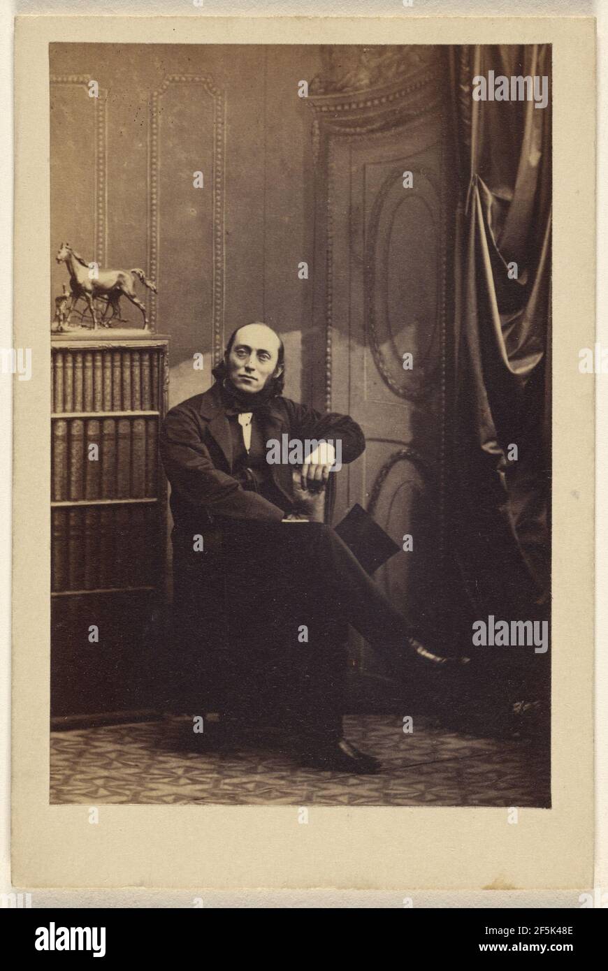 Unidentified man seated with his legs crossed, holding a top hat ...