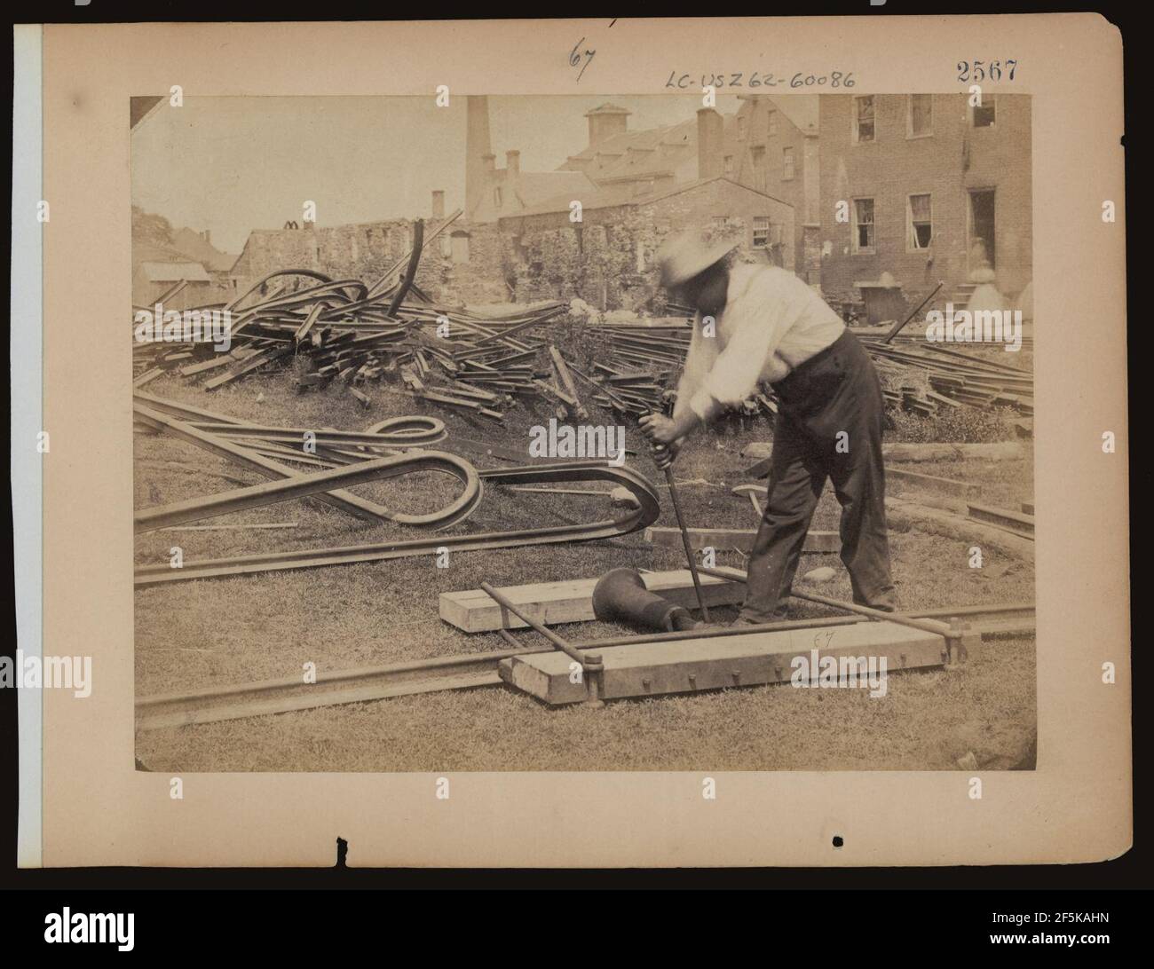 Railroad construction worker straightening track; pile of twisted rails ...