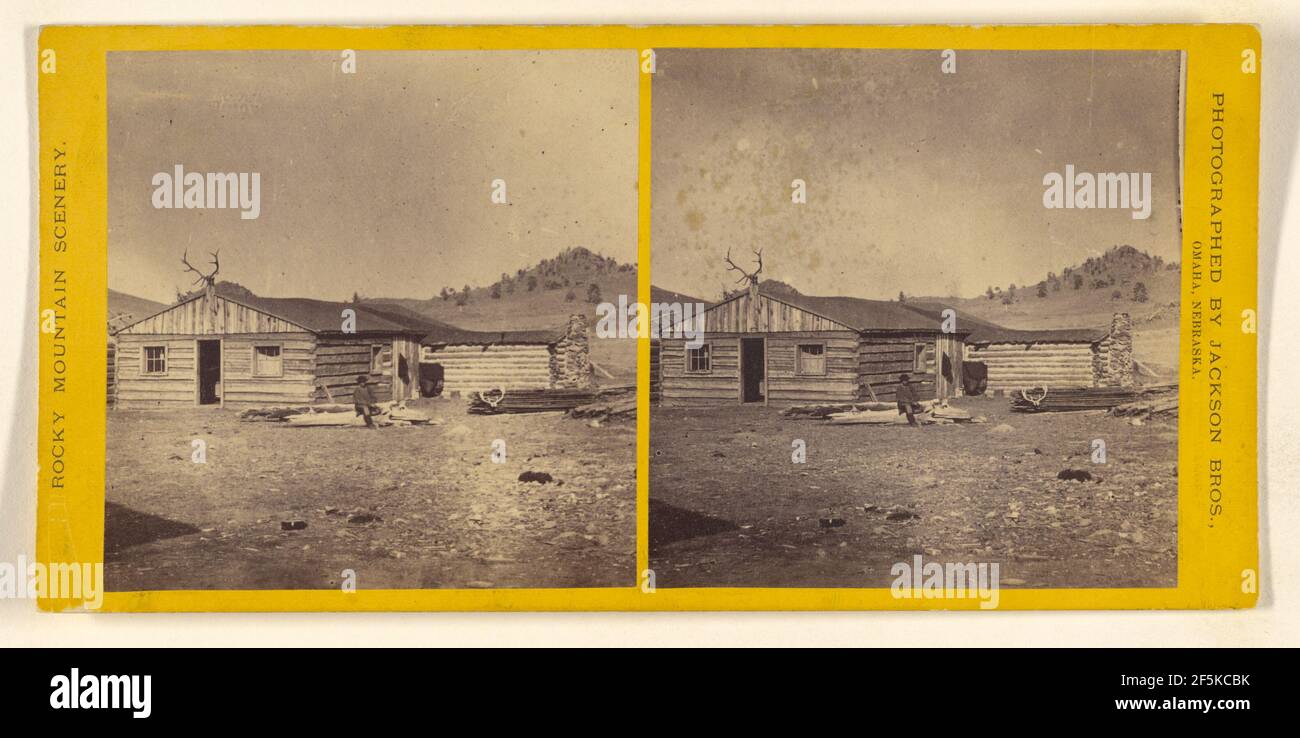 Log cabin, man seated on woodpile at front, antlers at crest of roof ...