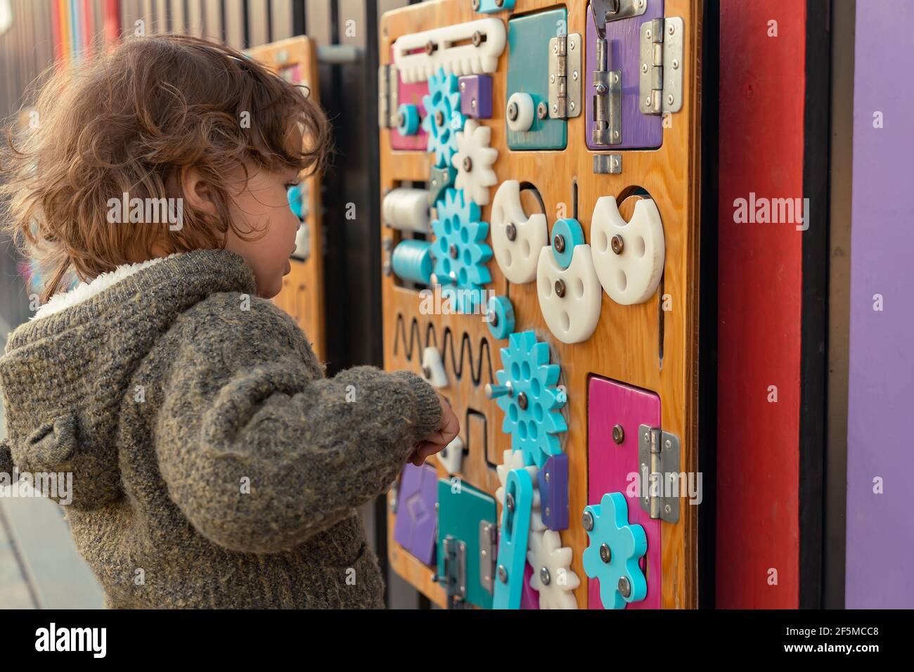 Portrait of a modern little boy playing with a busy board outdoors in ...