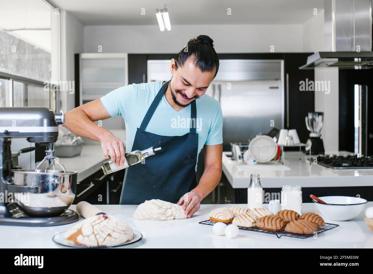 portrait of Latin man standing in kitchen baking and holding Conchas ...
