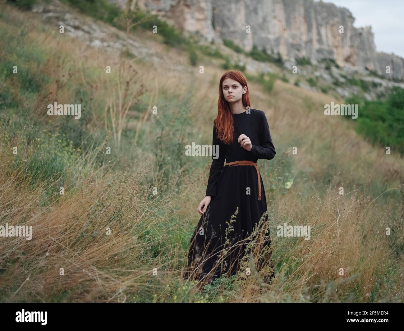 Traveler in the woods on a meadow in the mountains black dress red hair ...