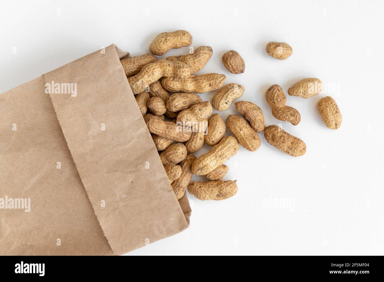 Peanuts in a shell spills out of a paper bag into a white background ...
