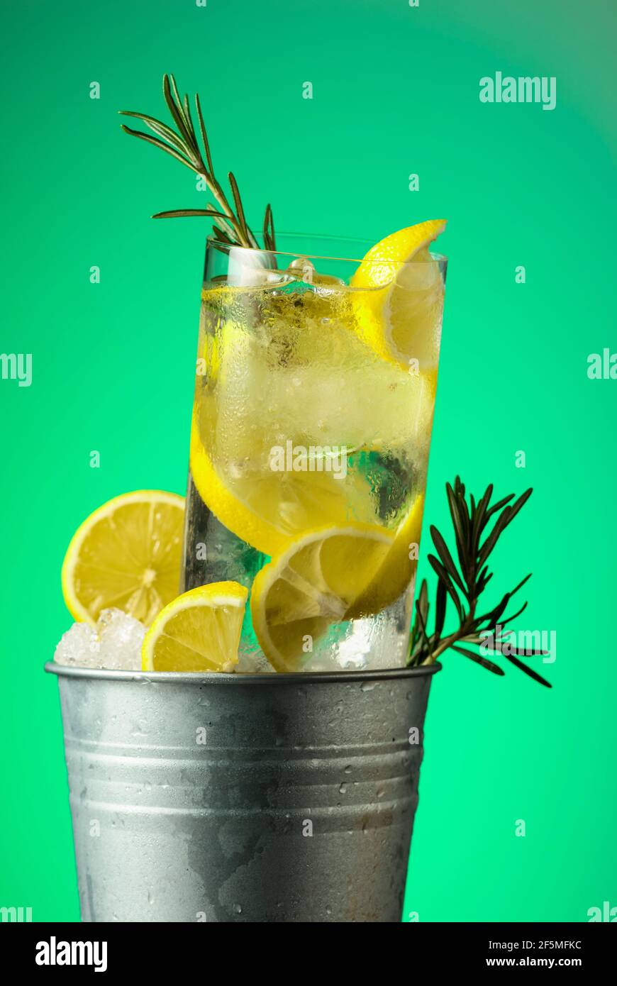 Gin-tonic cocktail with ice, lemon, and rosemary in a metal bucket with ...