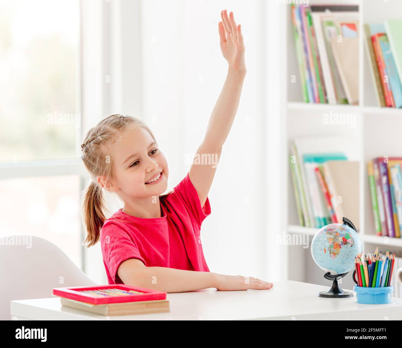 Smiling schoolgirl raising hand during lesson Stock Photo - Alamy