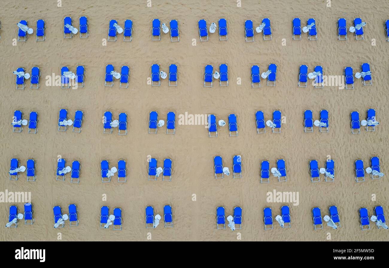 Aerial top view of a beach with white umbrellas and blue lounge chairs ...
