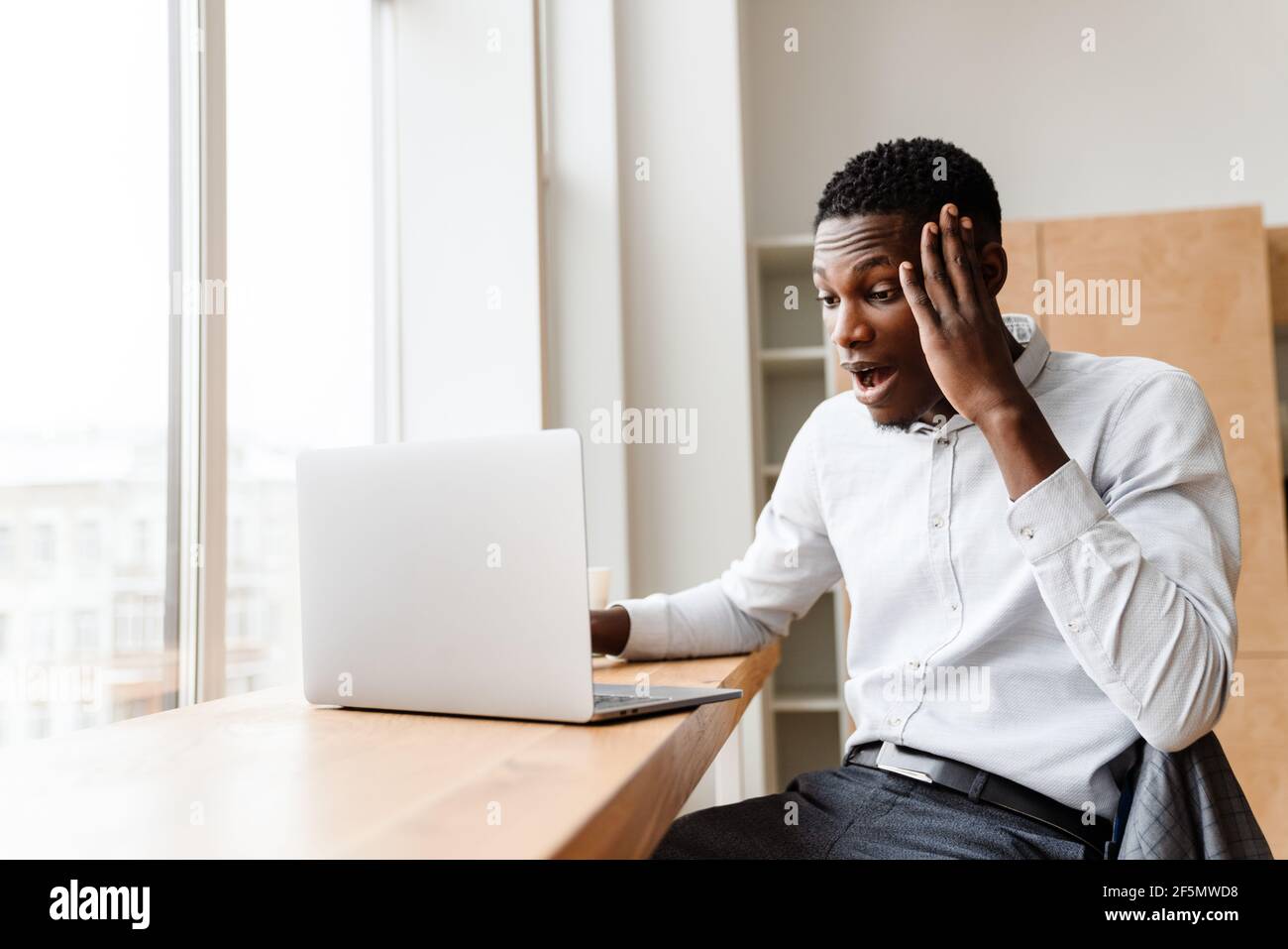 Afro american shocked man expressing surprise while working with laptop ...