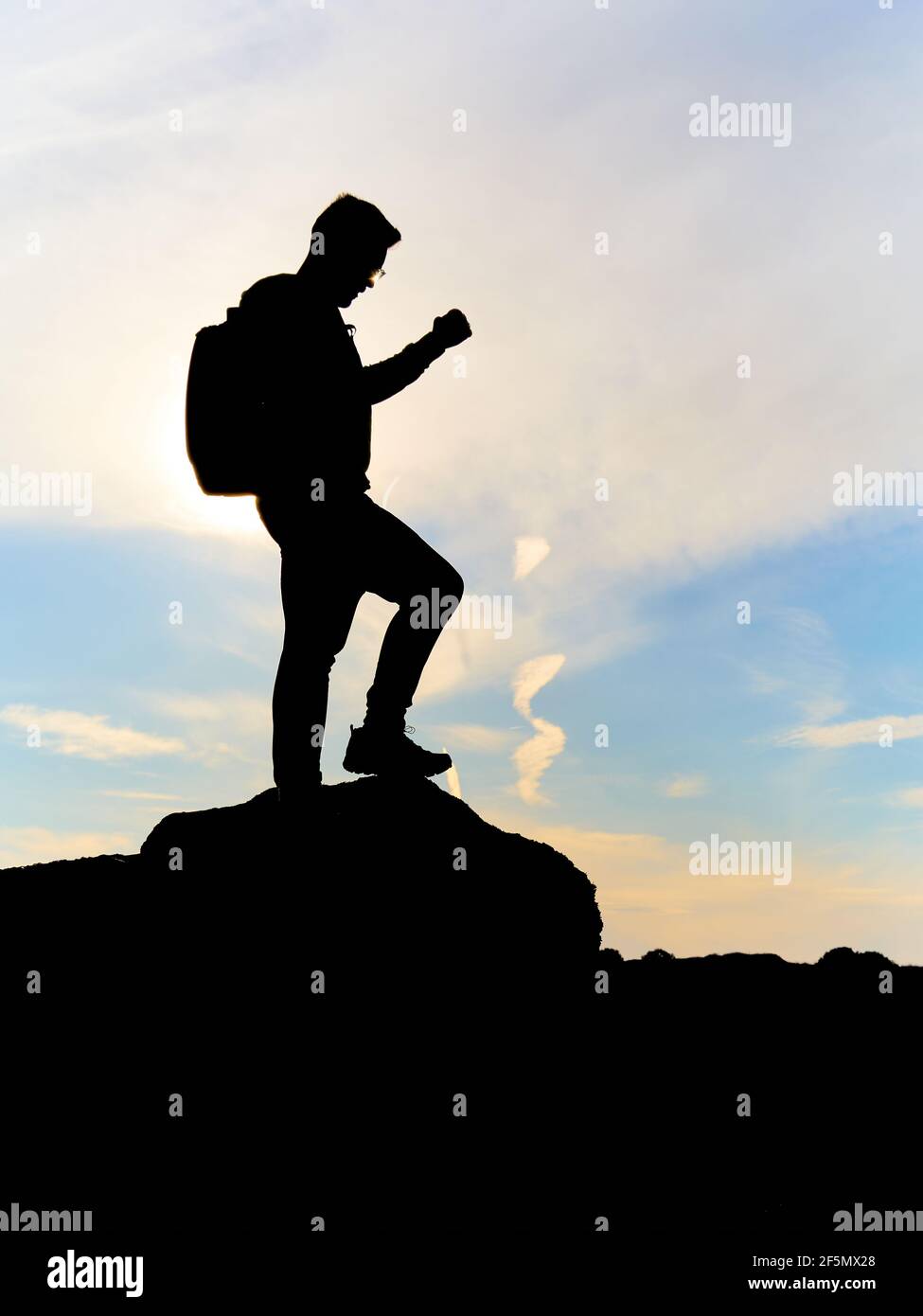 Silhouette of a man with one arm raised and backpack. Looking down ...