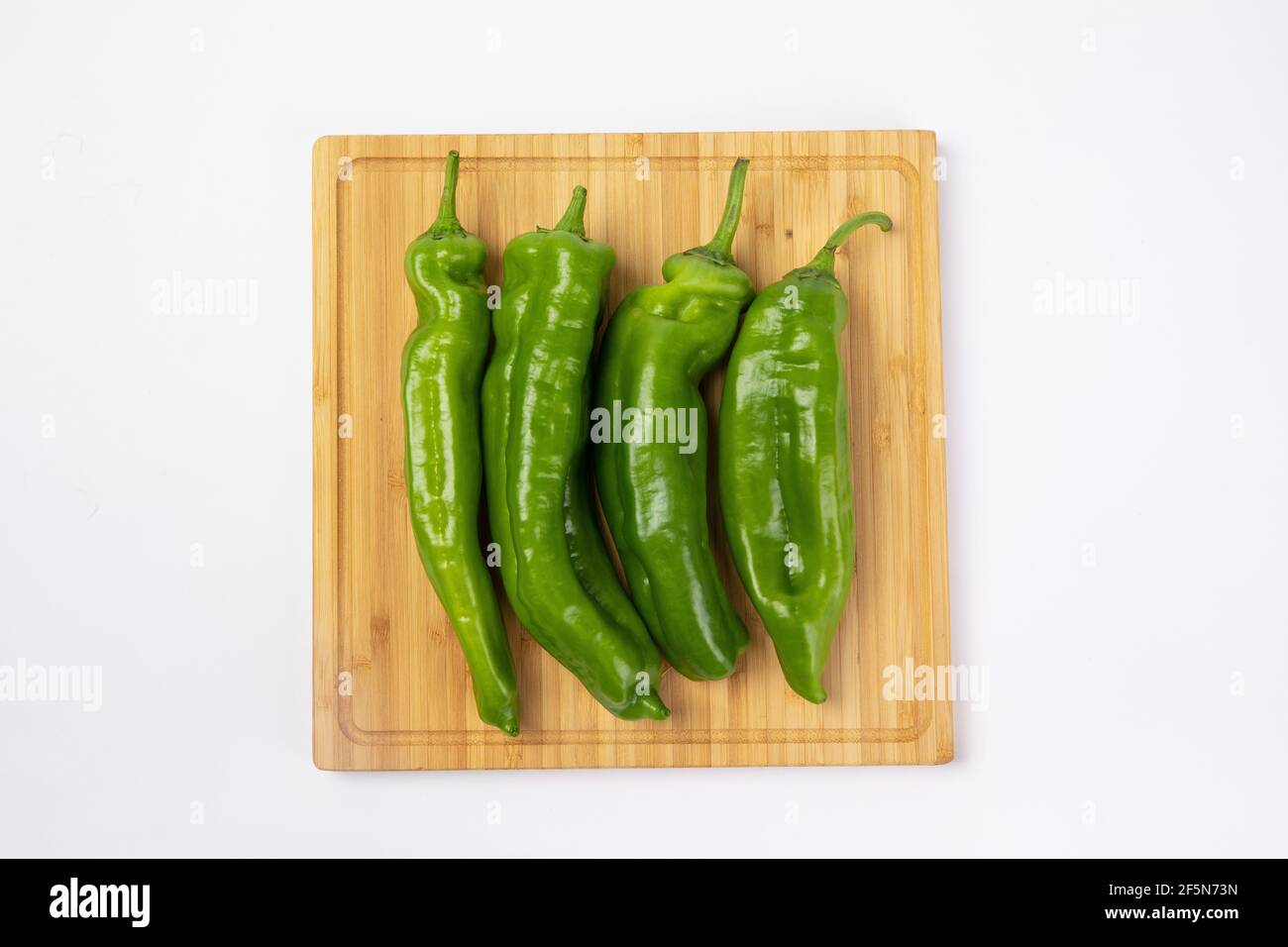 Top view of green peppers on a wooden board against white background ...