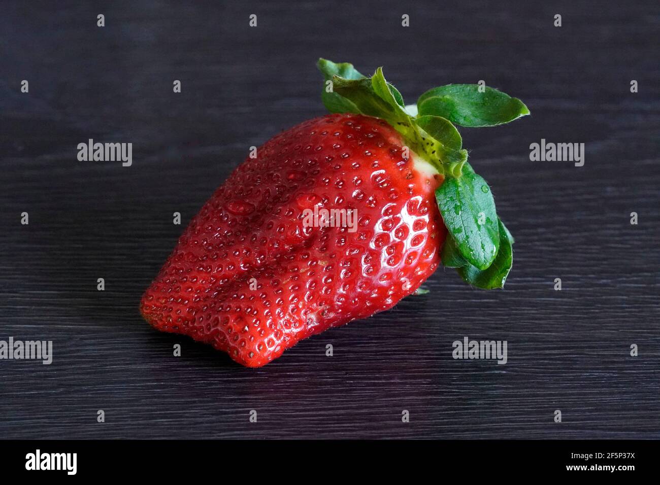 Single red ripe strawberry with green leaf. Fruit on dark background ...