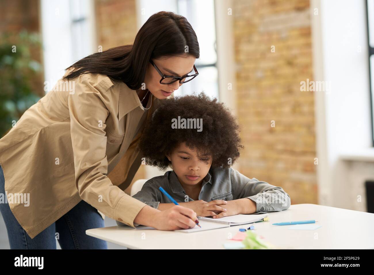 Guiding young female teacher in glasses helping little boy with the ...