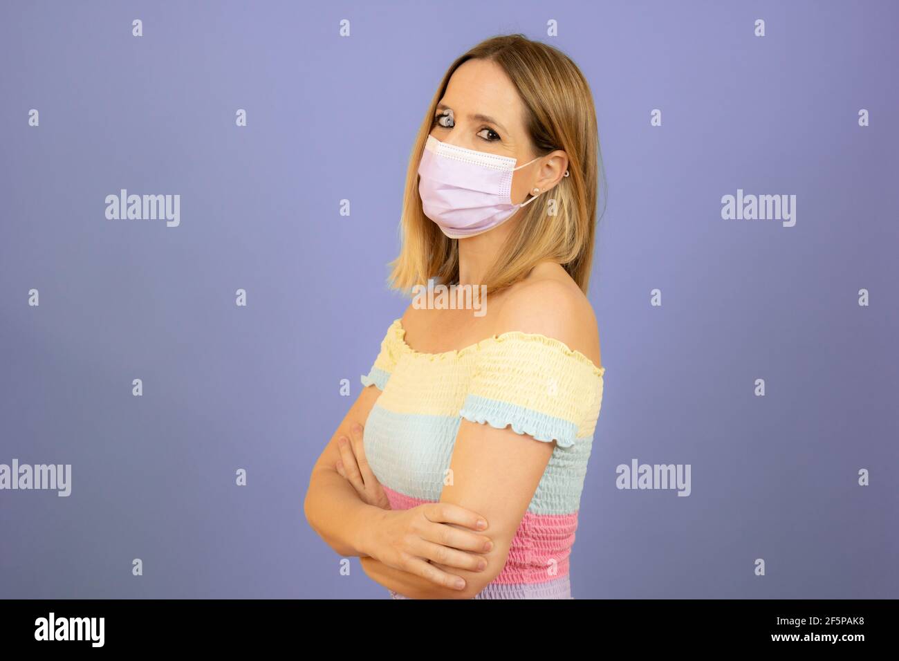 Young woman wearing surgical mask with arms folded isolated over purple ...
