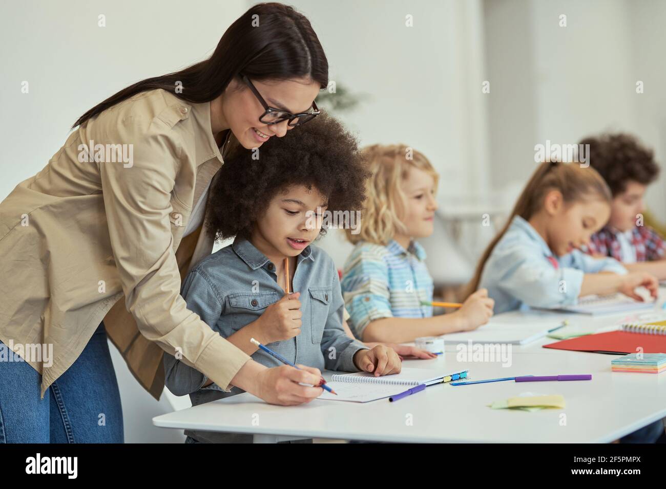 Helpful young female teacher showing how to do task to little schoolboy ...