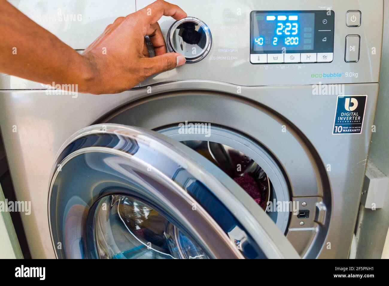 Adult middle aged Asian man adjusting the round knob of washing machine ...