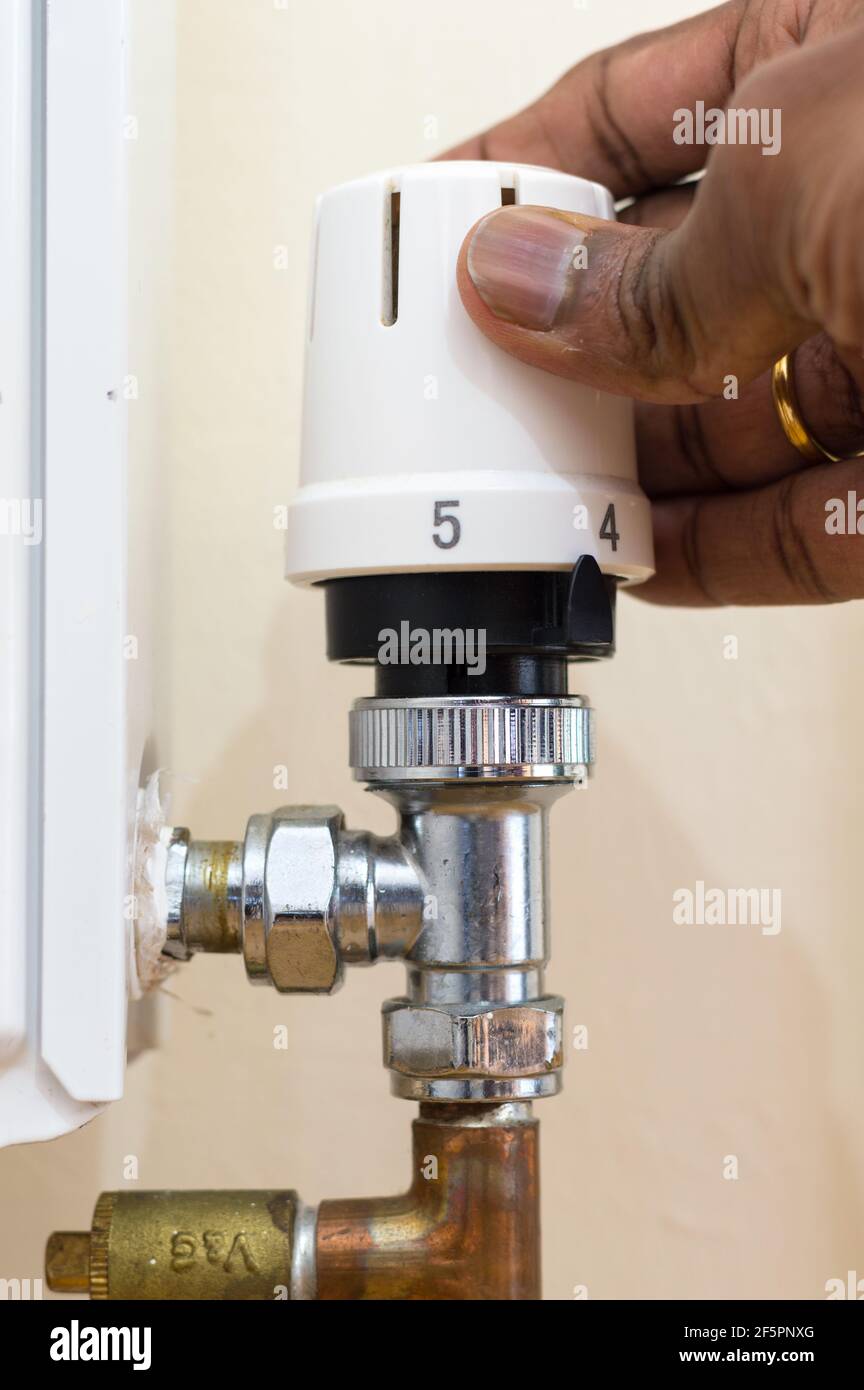 Asian man adjusting room temperature on a home thermostat to reduce the ...