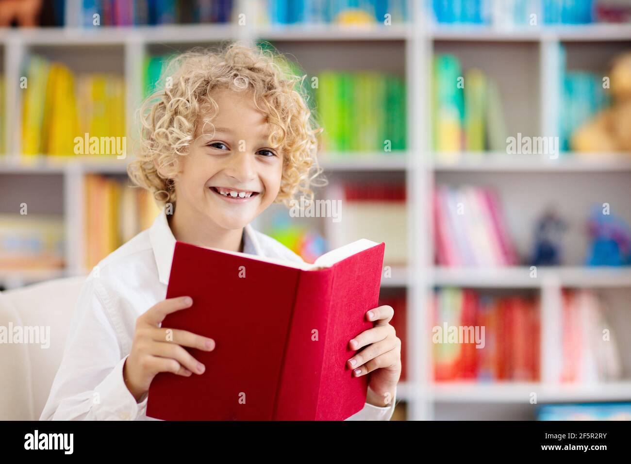 Child reading book. Kids read. Little boy at a colorful bookshelf doing ...