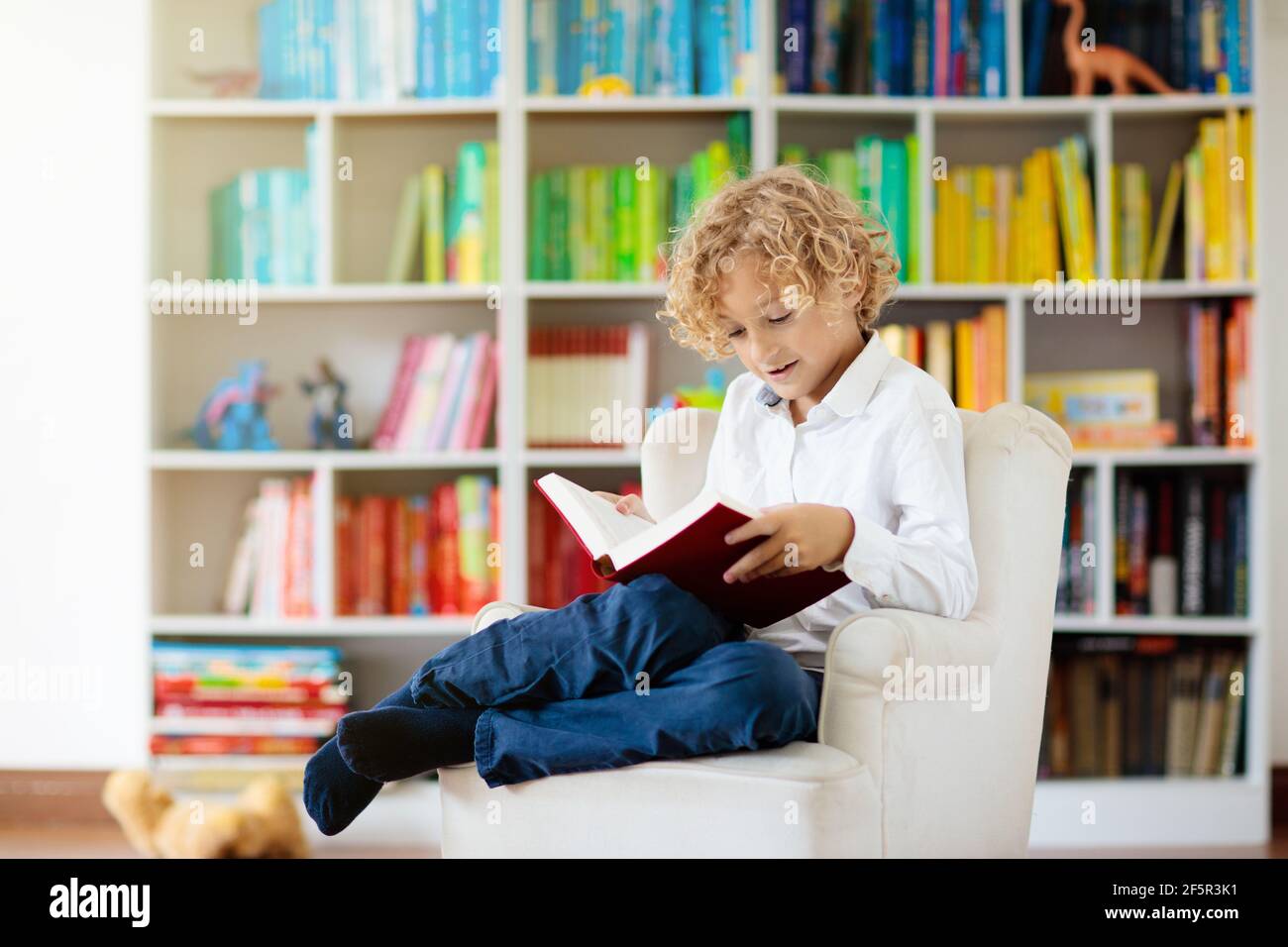 Child reading book. Kids read. Little boy at a colorful bookshelf doing ...