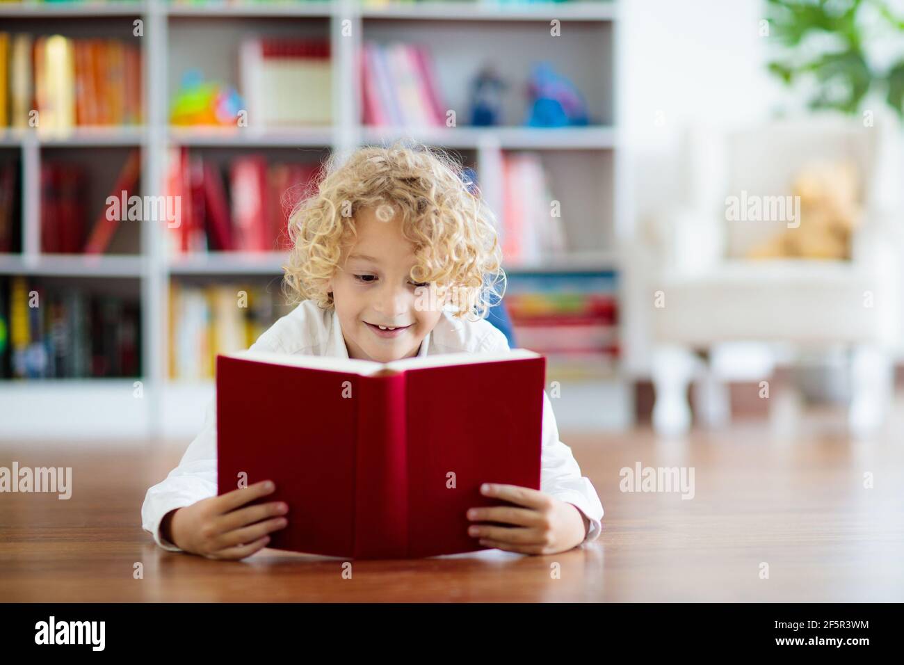 Child reading book. Kids read. Little boy at a colorful bookshelf doing ...