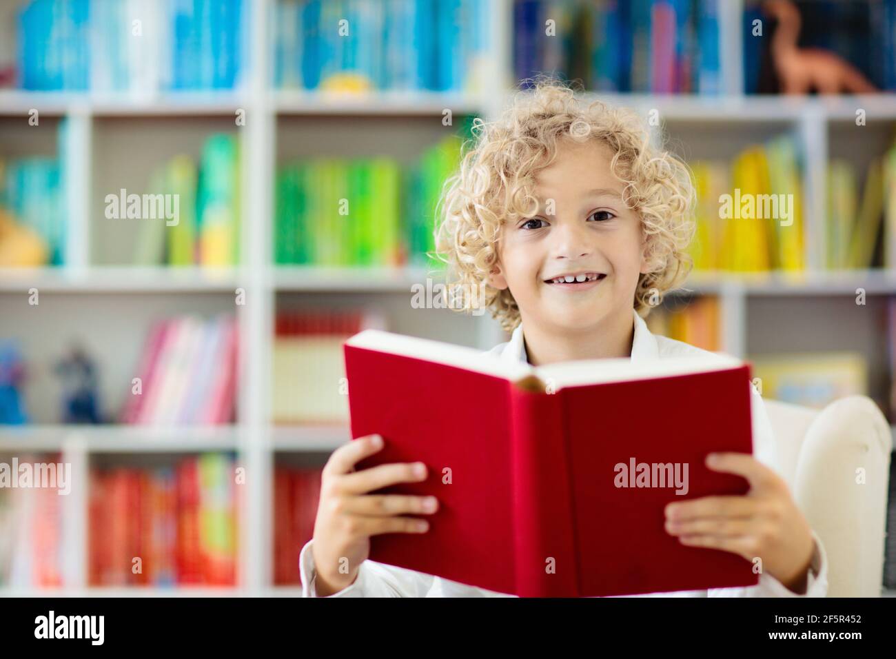 Child reading book. Kids read. Little boy at a colorful bookshelf doing ...